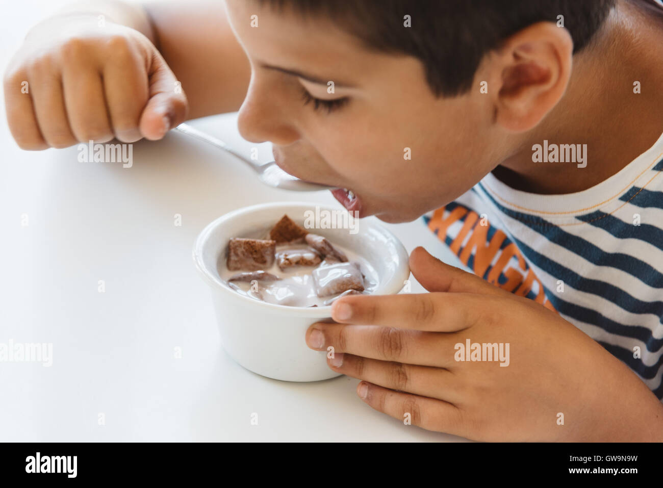 Boy eating yoghurt with cereals on white table Stock Photo - Alamy