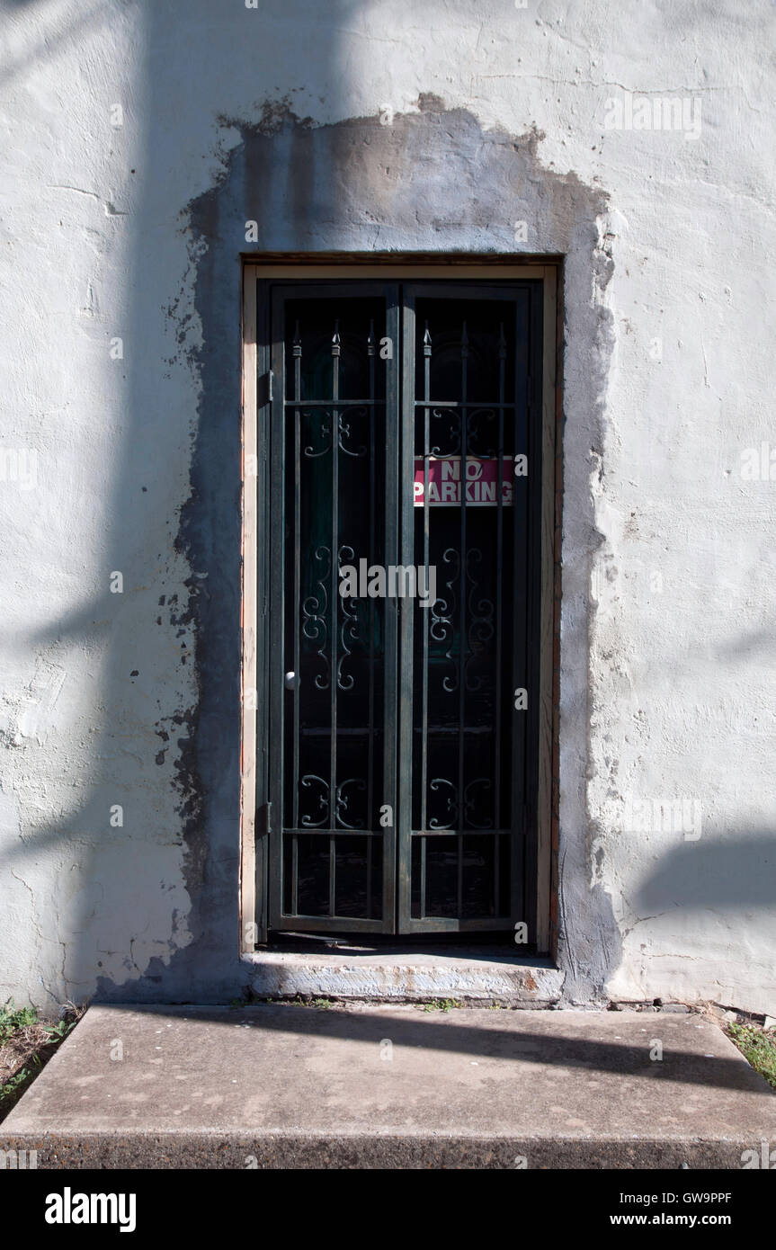 Distressed door behind an iron security gate with a "No Parking" sign ...