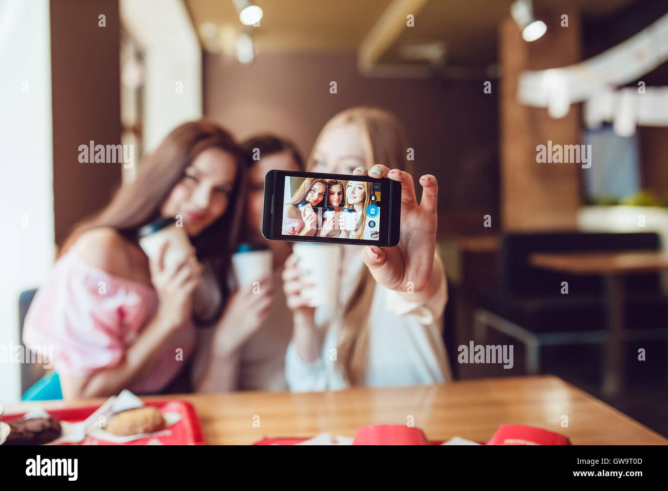 Three young girls are doing selfie in fast food restaurant Stock Photo ...