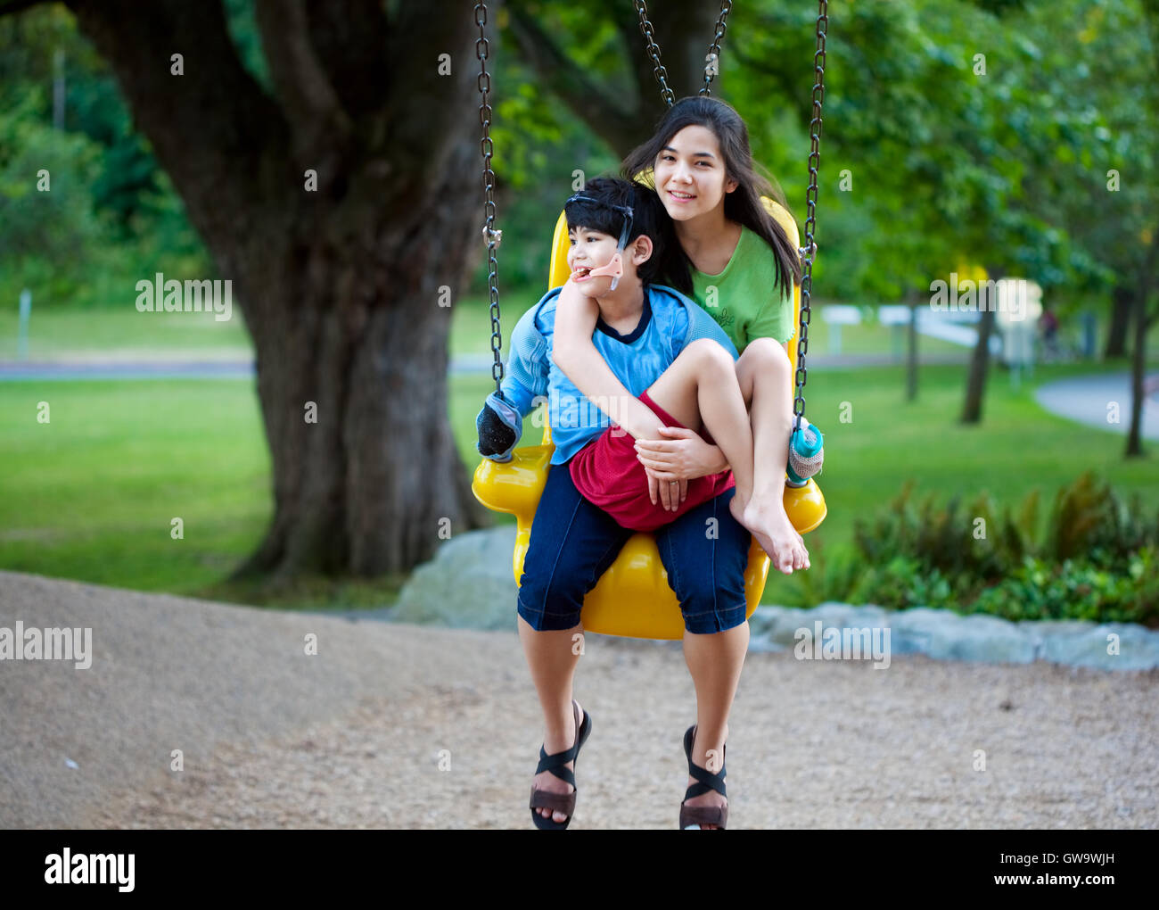 Big sister holding disabled brother on special needs swing at pl Stock ...