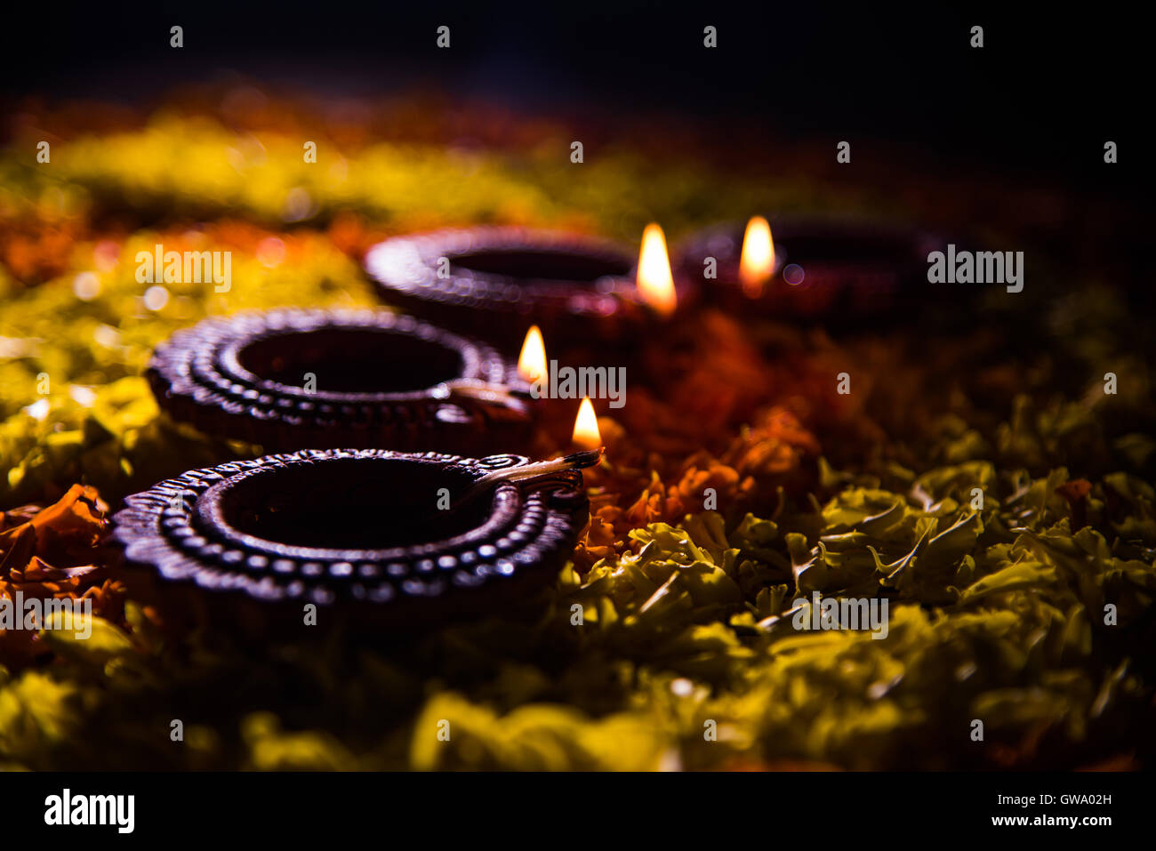 Traditional diya or oil lamp lit on colorful rangoli made up of flower ...