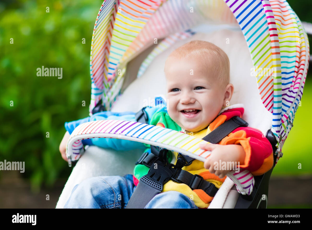 Baby boy in white sweater sitting in white stroller on walk in a park ...