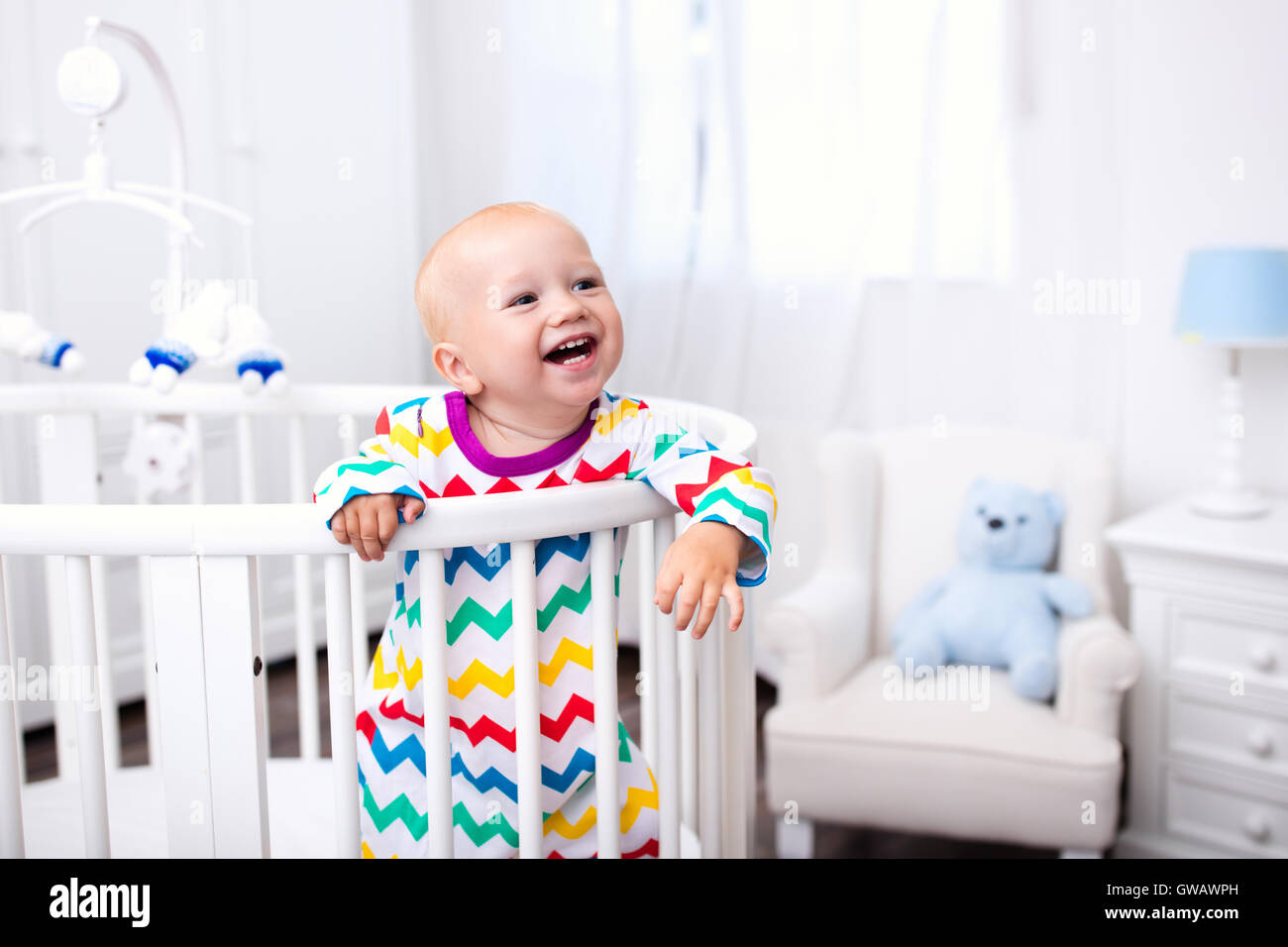 Cute laughing baby standing in bed after nap time. Nursery interior for ...