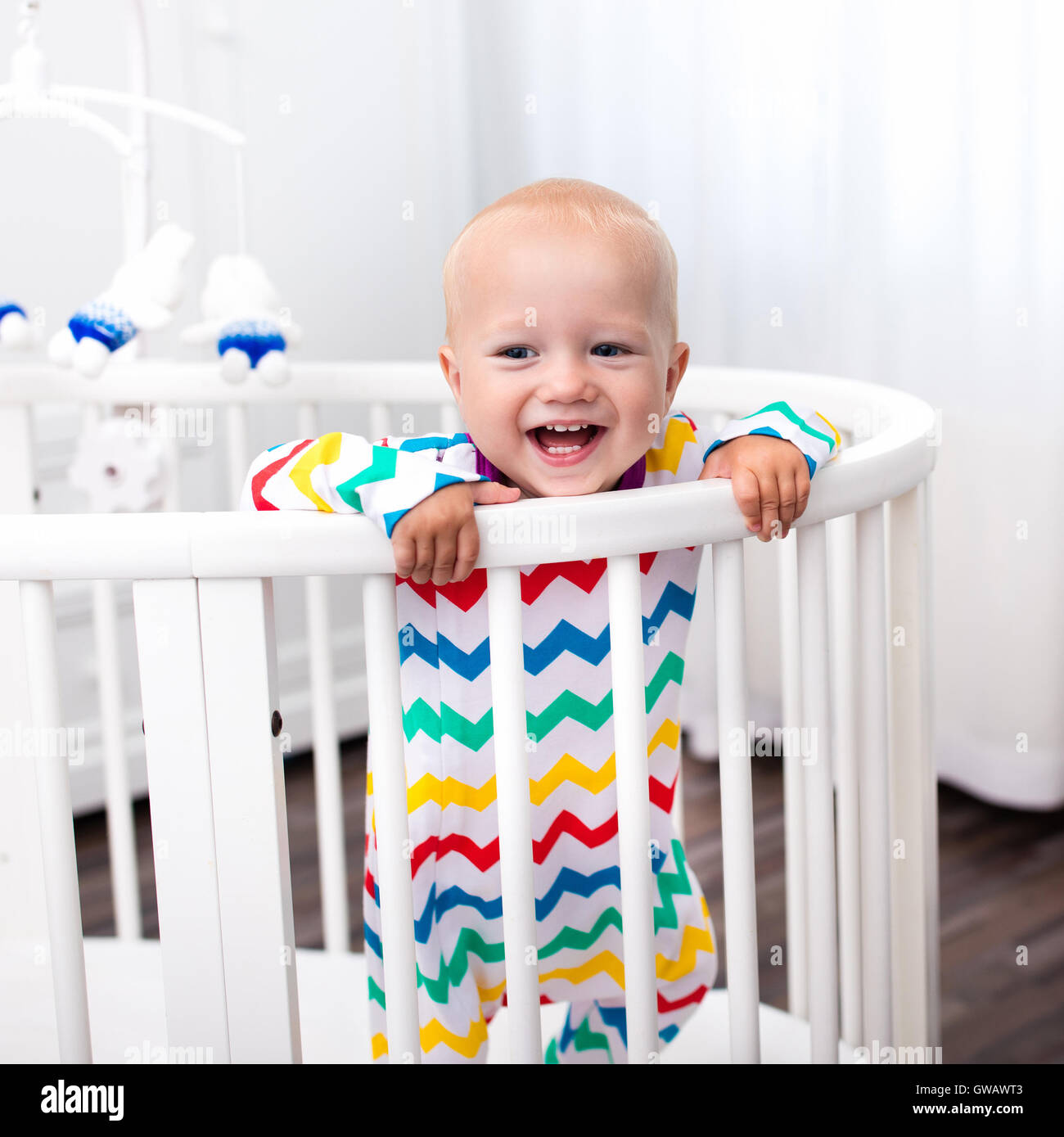 Cute laughing baby standing in bed after nap time. Nursery interior for ...
