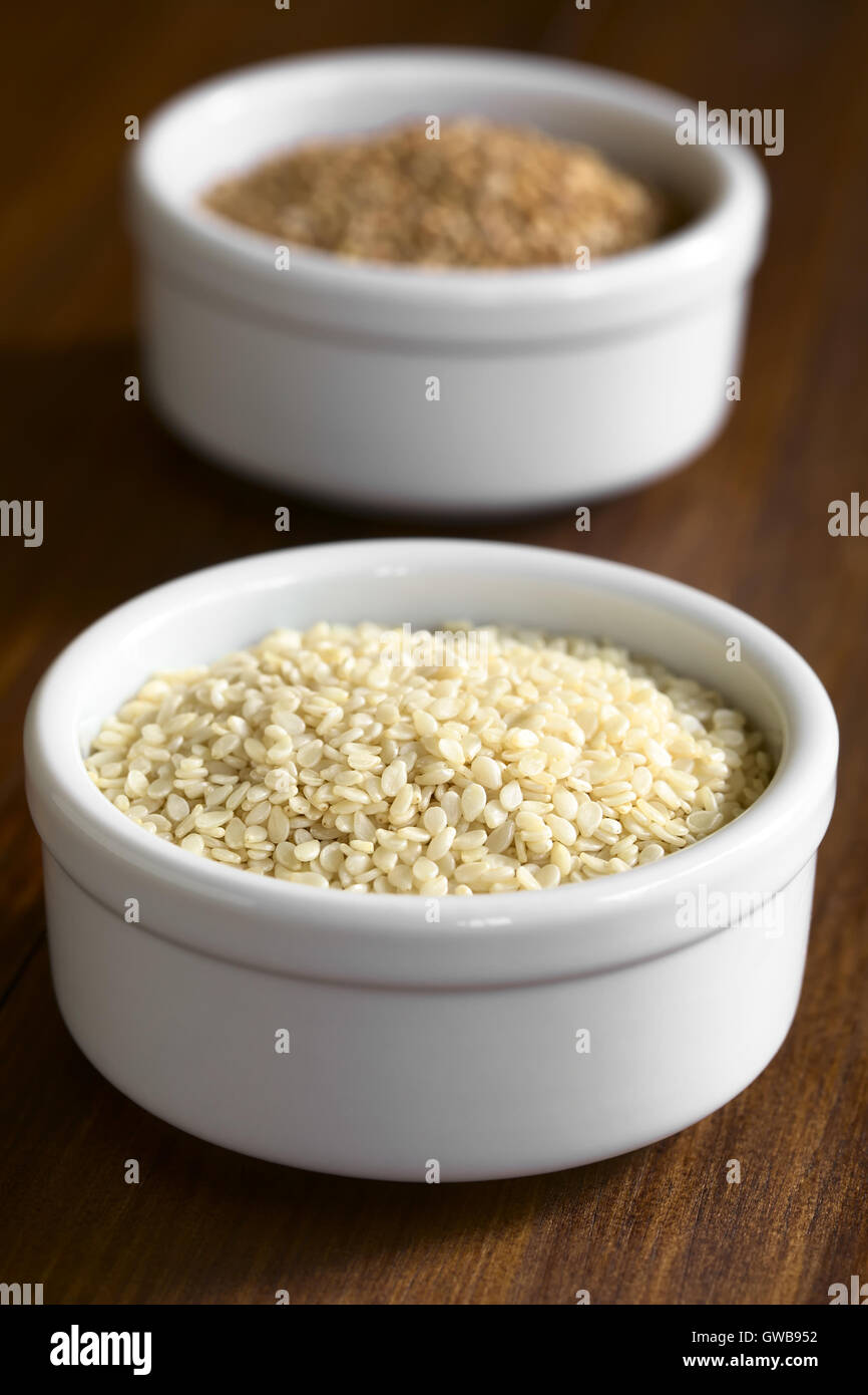 White and roasted sesame seeds in small bowls, photographed with ...