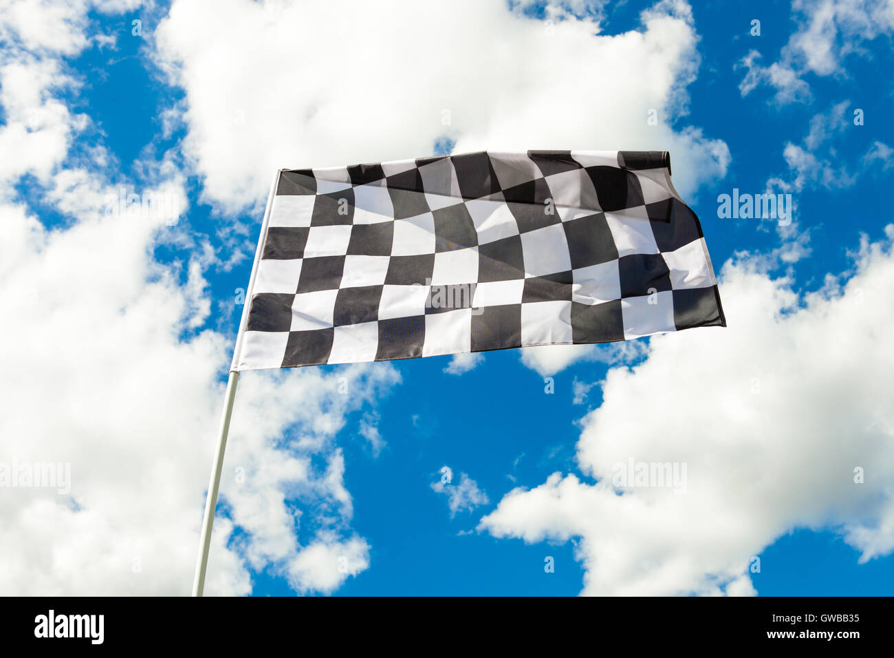 Checkered flag on flagpole waving in the wind with clouds on background ...