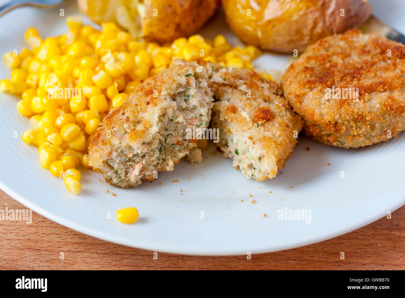 A salmon fishcake, cut open, served with sweetcorn on a white plate ...
