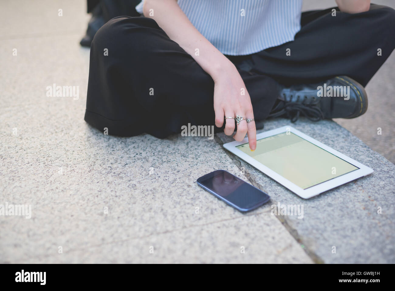From the neck down view of young beautiful woman sitting on a sidewalk ...