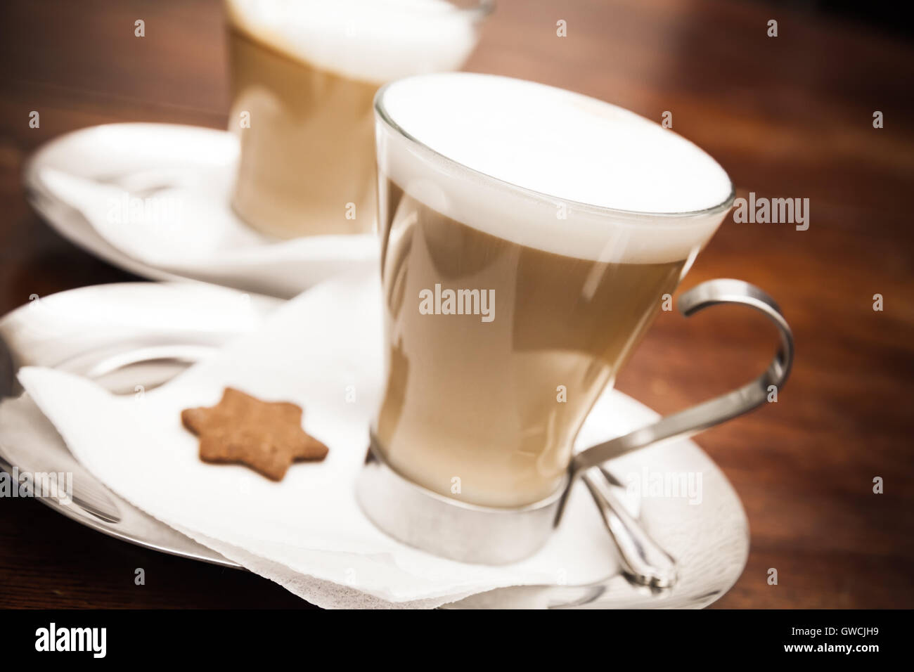 Glass mugs full of Cappuccino coffee stand on wooden table in cafeteria ...