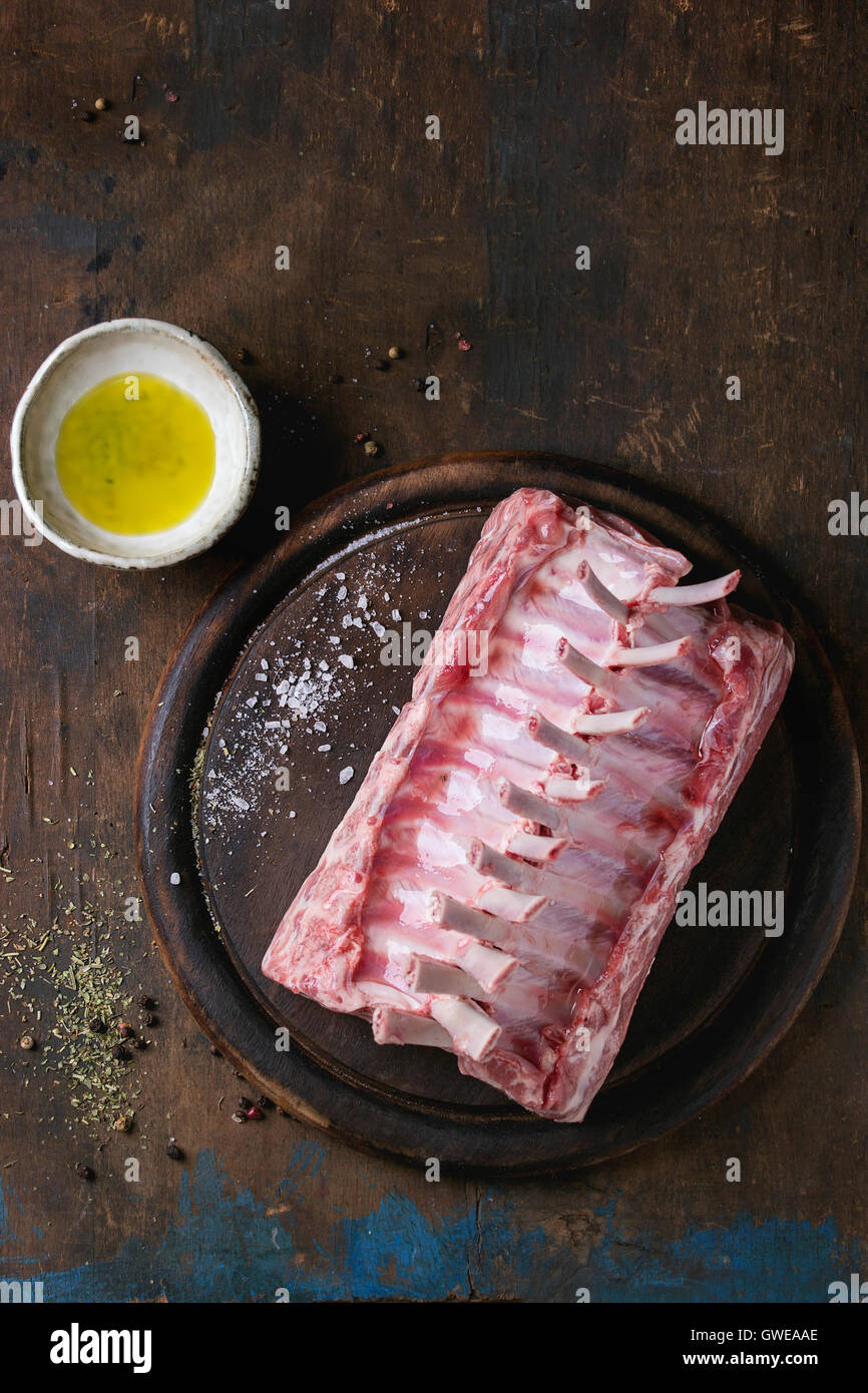 Raw uncooked rack of lamb on wood chopping board with salt, pepper, dry ...