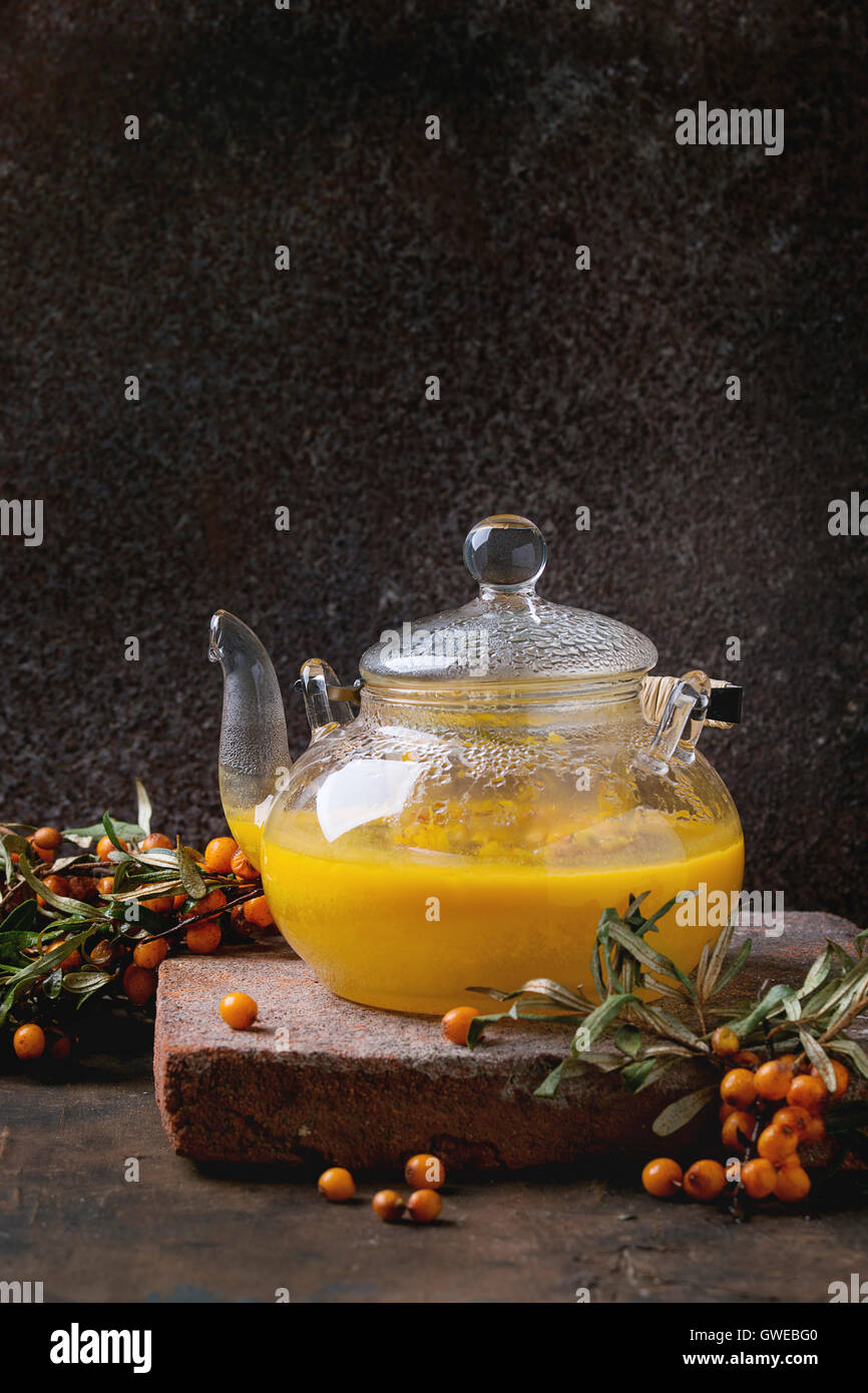 Hot berry sea buckthorn tea drink with apples in glass teapot on clay ...