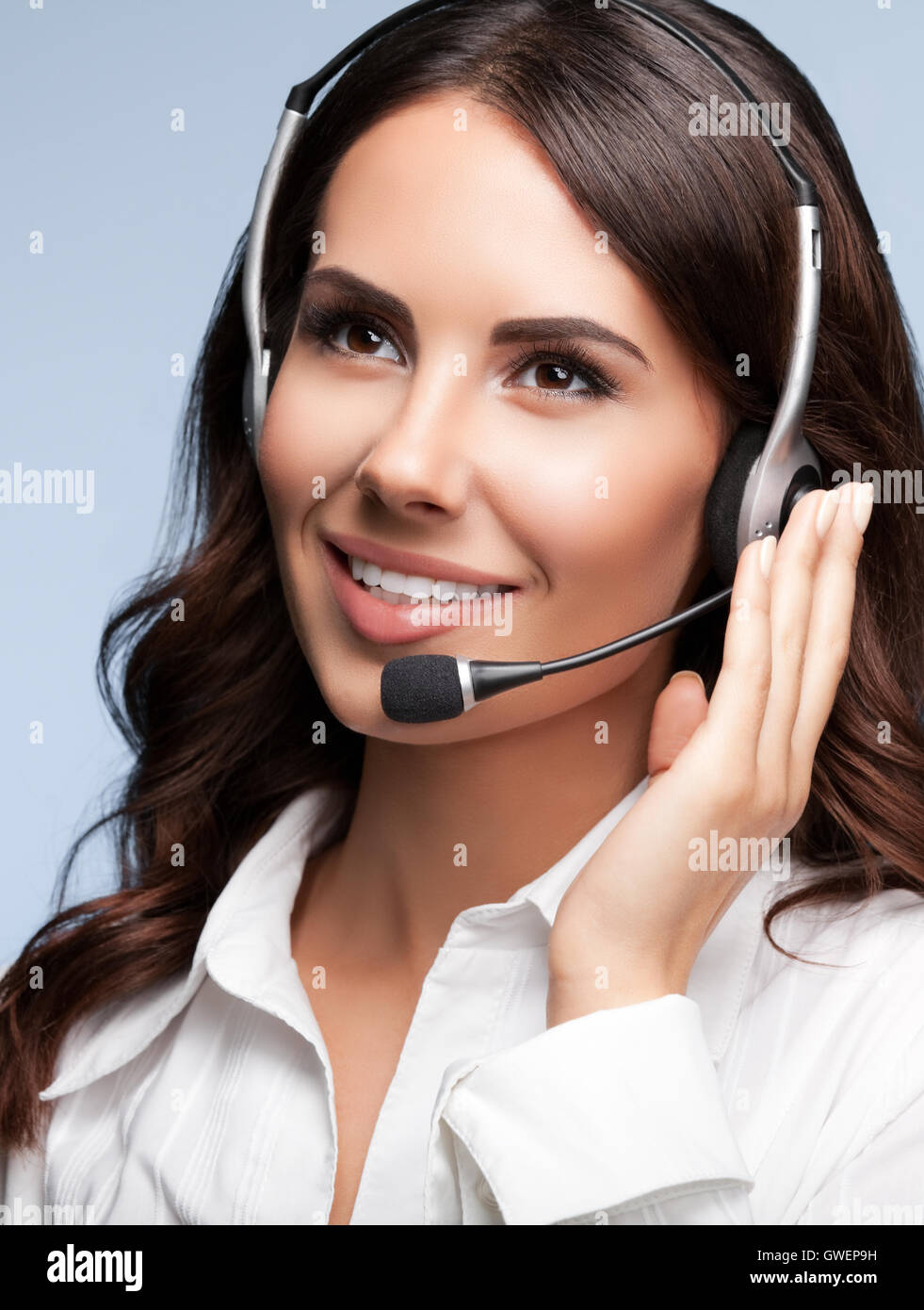 cheerful customer support female phone operator in headset, against grey background. Consulting ...