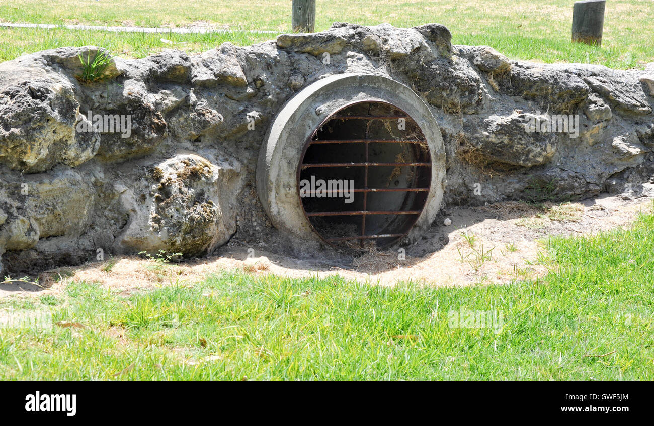 Rocky culvert with pipe covered with rusted metal grate in ditch with ...