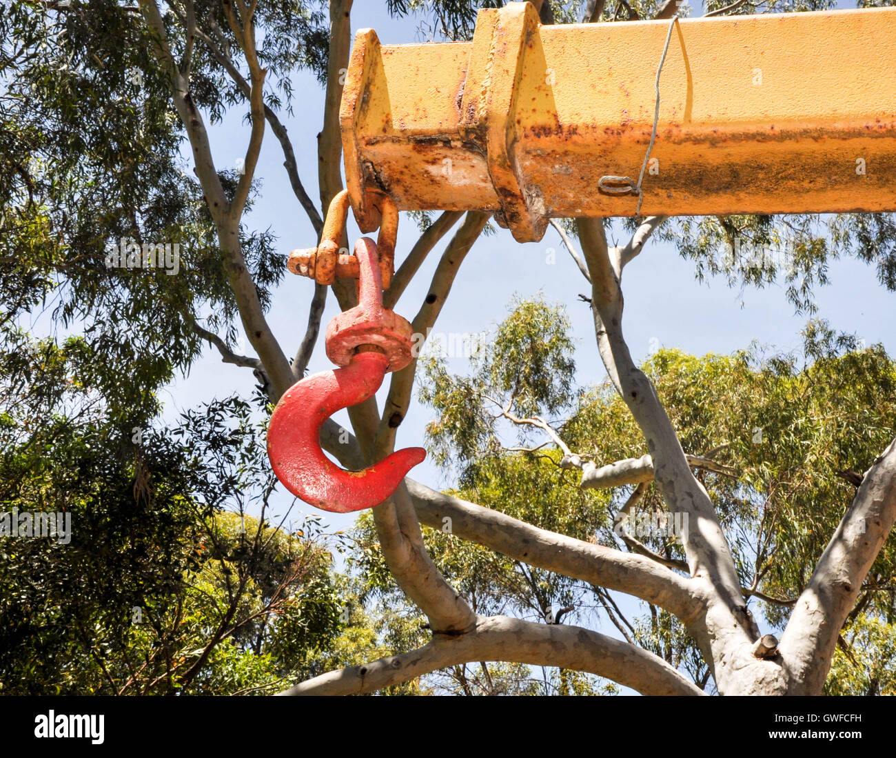 Large red industrial hook hanging from old yellow farm machinery with ...