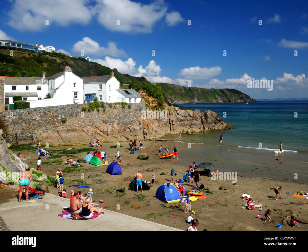 Holidaymakers sitting on a Cornish beach with white painted cottages ...