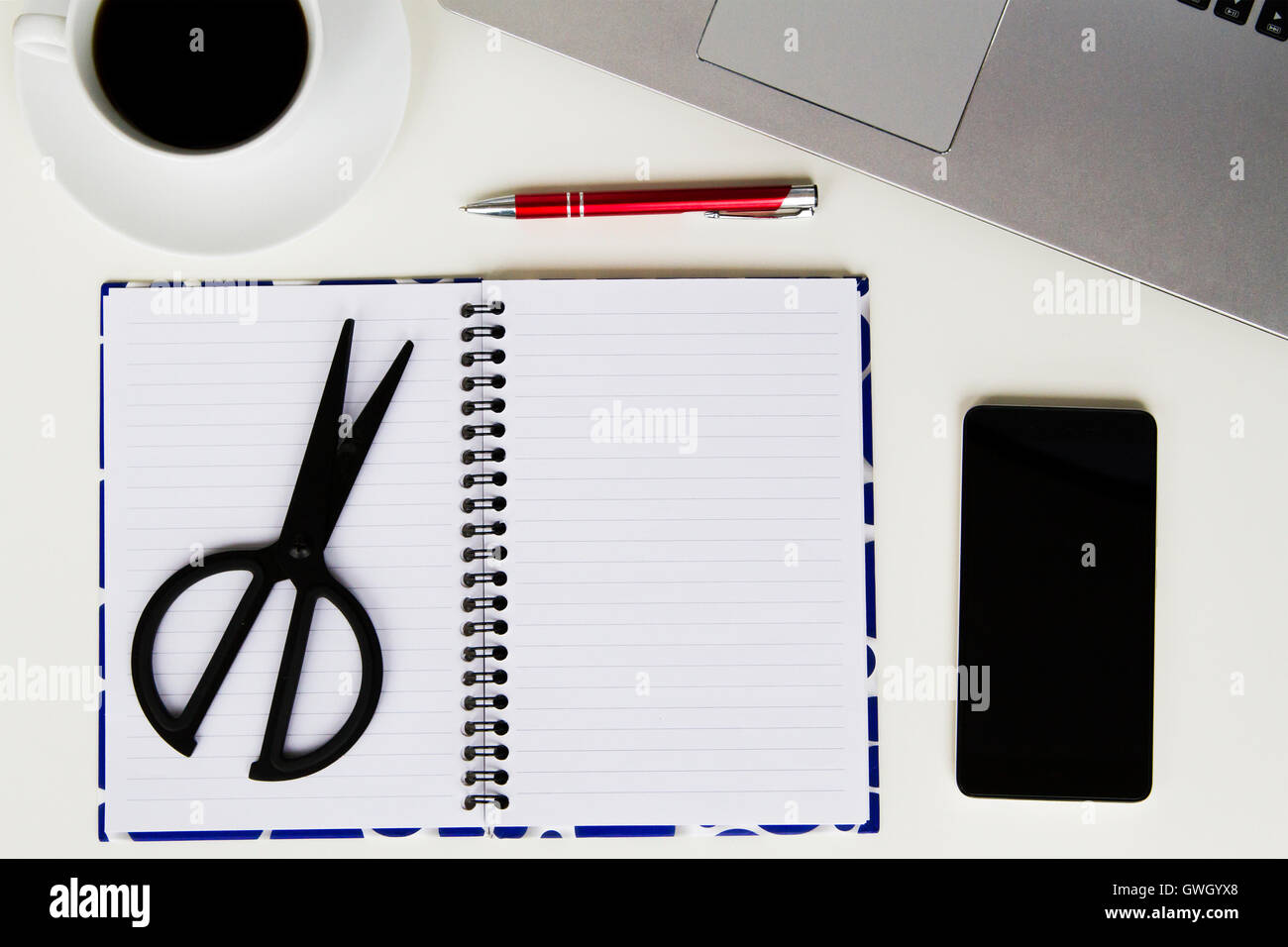 White desk with laptop keyboard, coffee mug, open colourful notebook ...