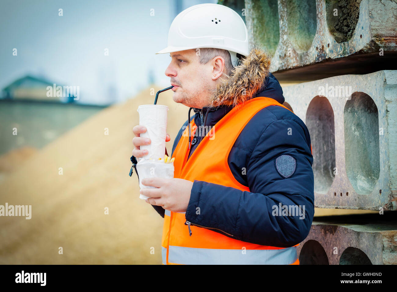 Worker drinking soda and eating french fries at construction site Stock ...