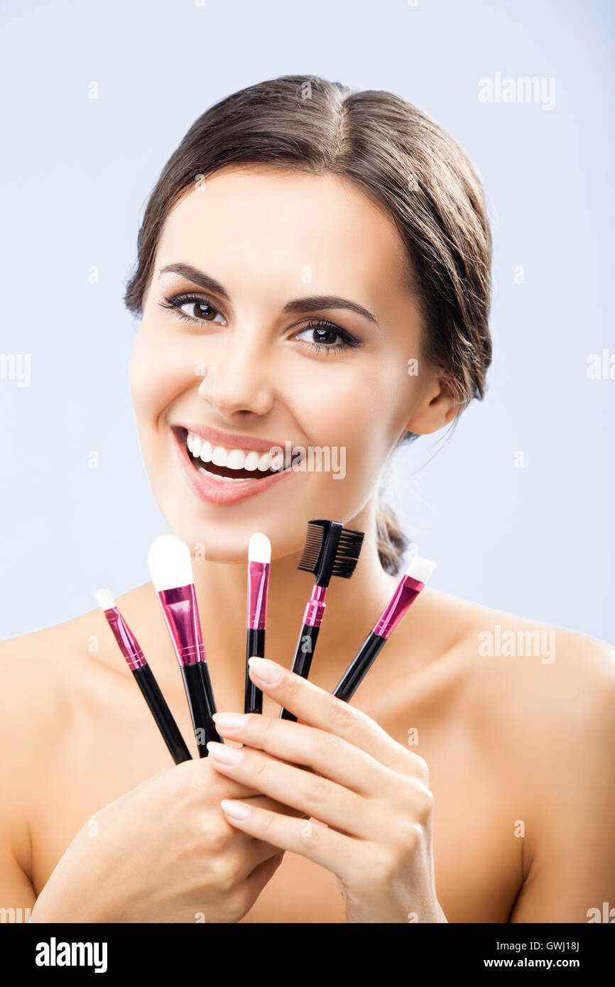 Young happy smiling woman with cosmetics make up tools, over grey ...