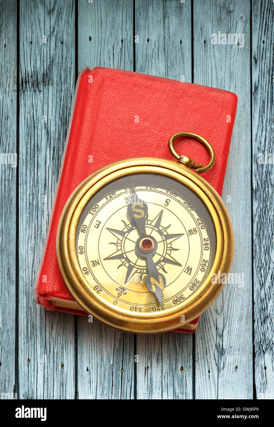 Red closed book with retro compass on wood Stock Photo - Alamy