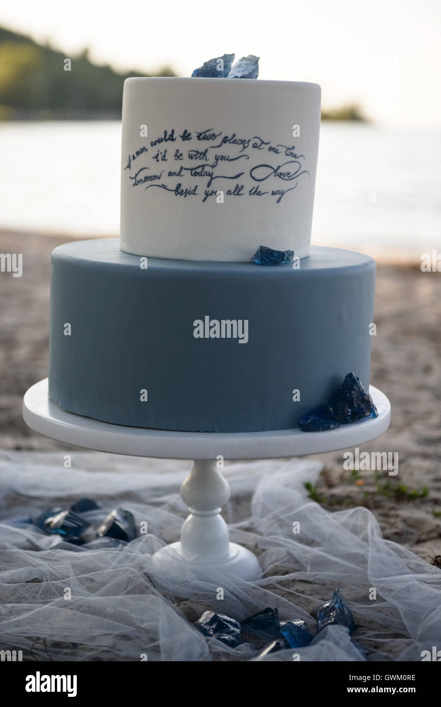 Blue two-tiered wedding cake on a sandy beach, decorated with blue ...