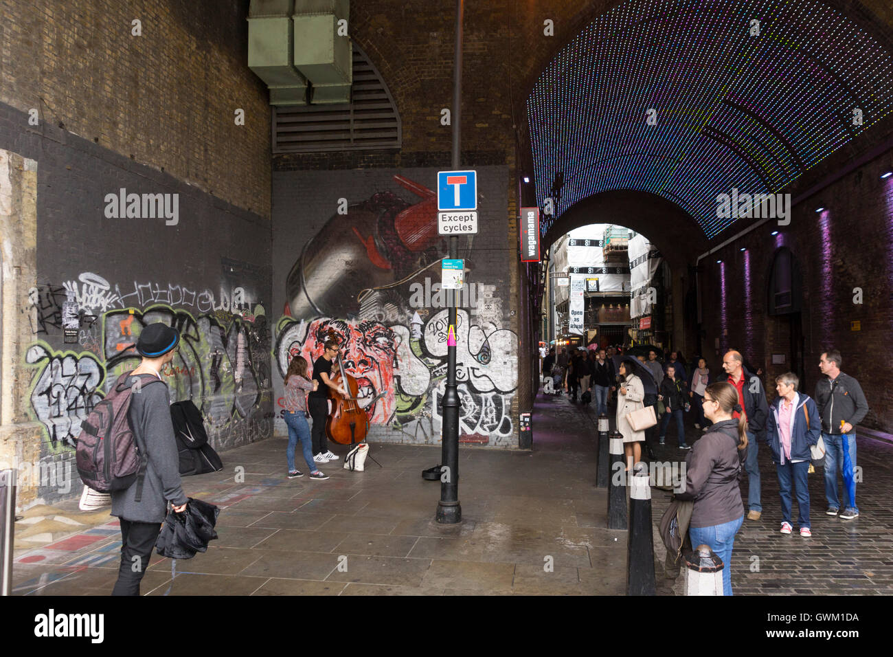 A pair of musicians busking on Clink Street, London, watched by a crowd ...