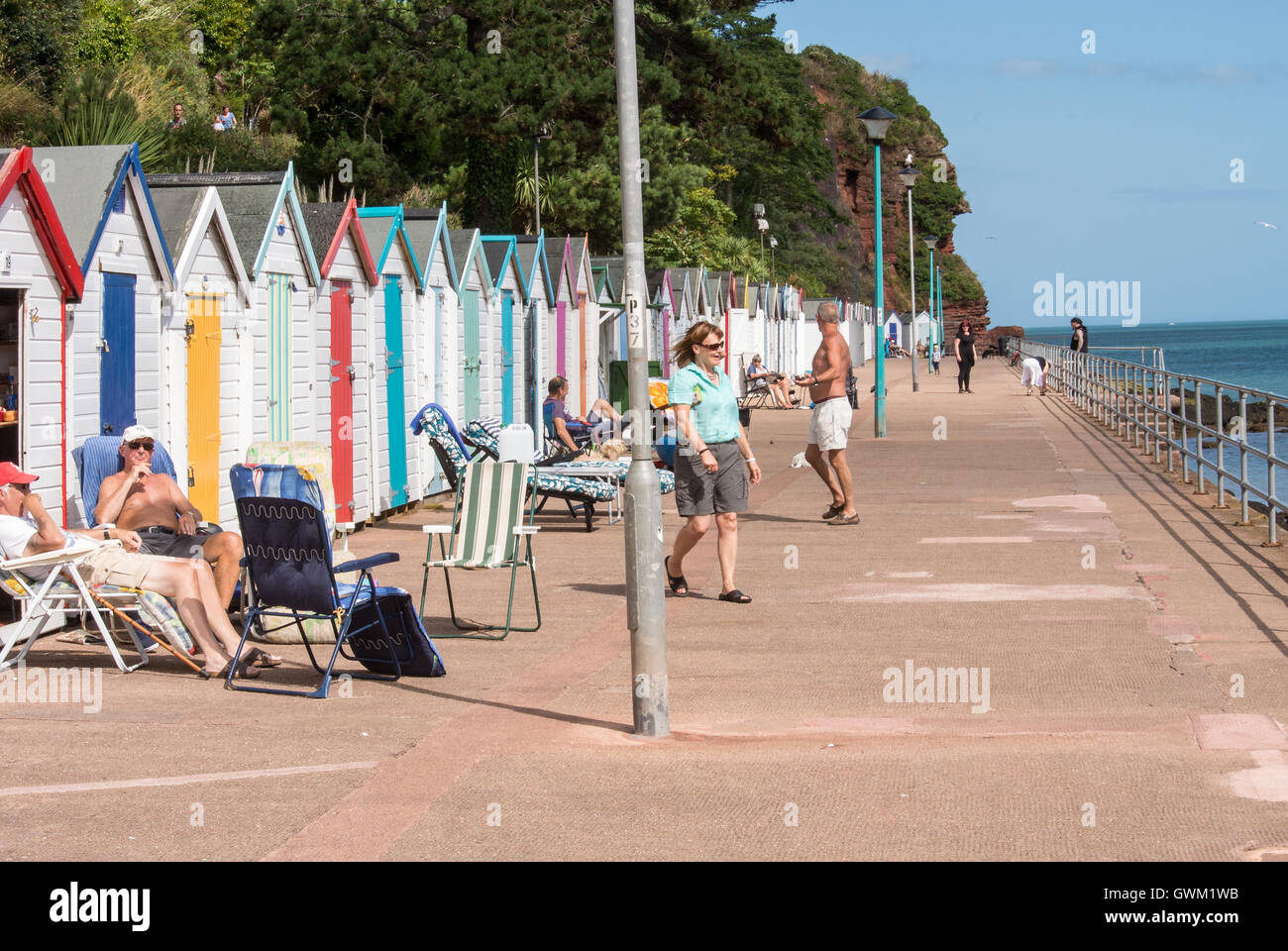 Holiday makers relax outside beach huts at Goodrington Sands on a ...