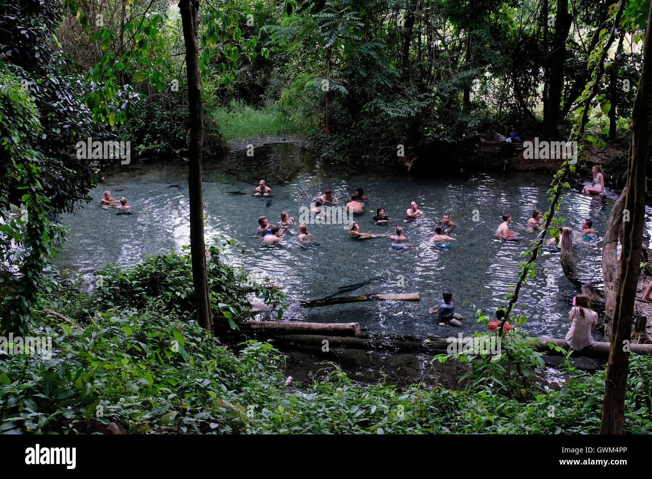 Tourists bath in the shallow lagoon of Sai Ngam Hot Springs surrounded ...