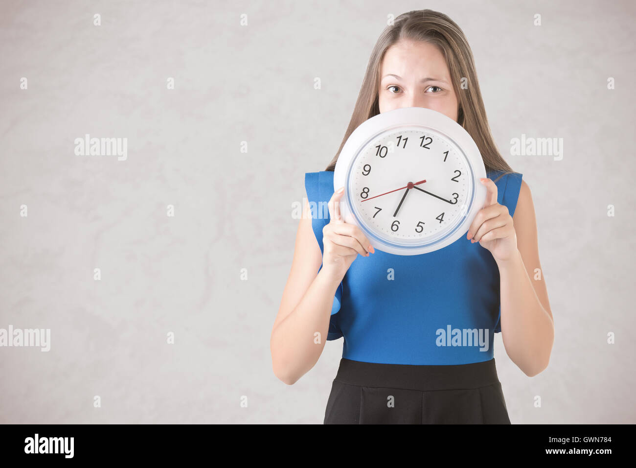 Woman hiding behind alarm clock. Isolated in grey Stock Photo - Alamy