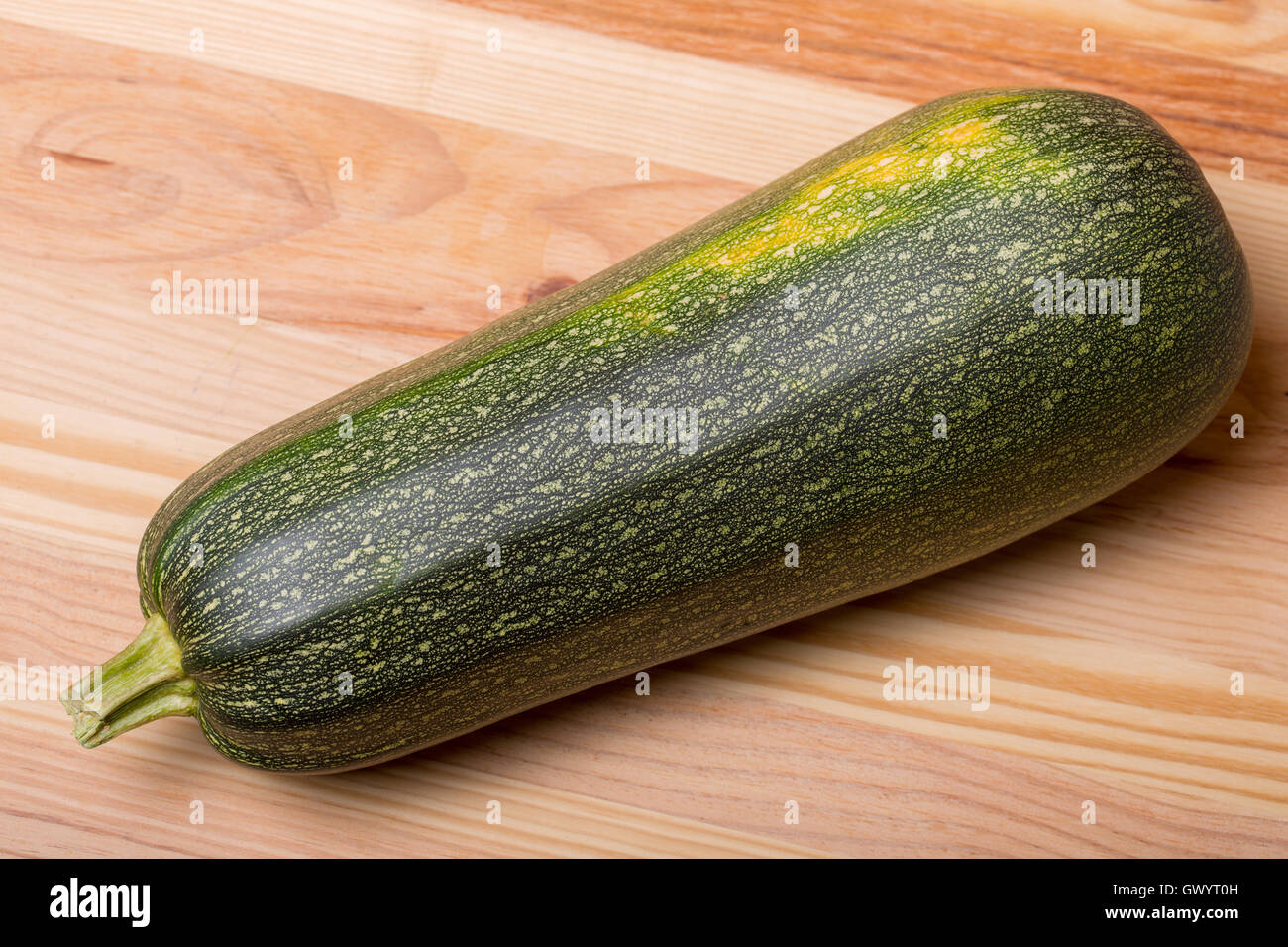 One green zucchini vegetable shown whole on a yellow wooden background ...