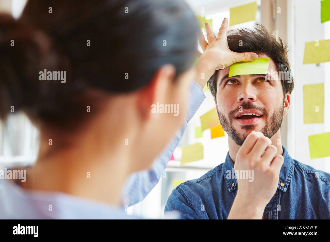 Young man in team building game with sticky note on forehead having an ...