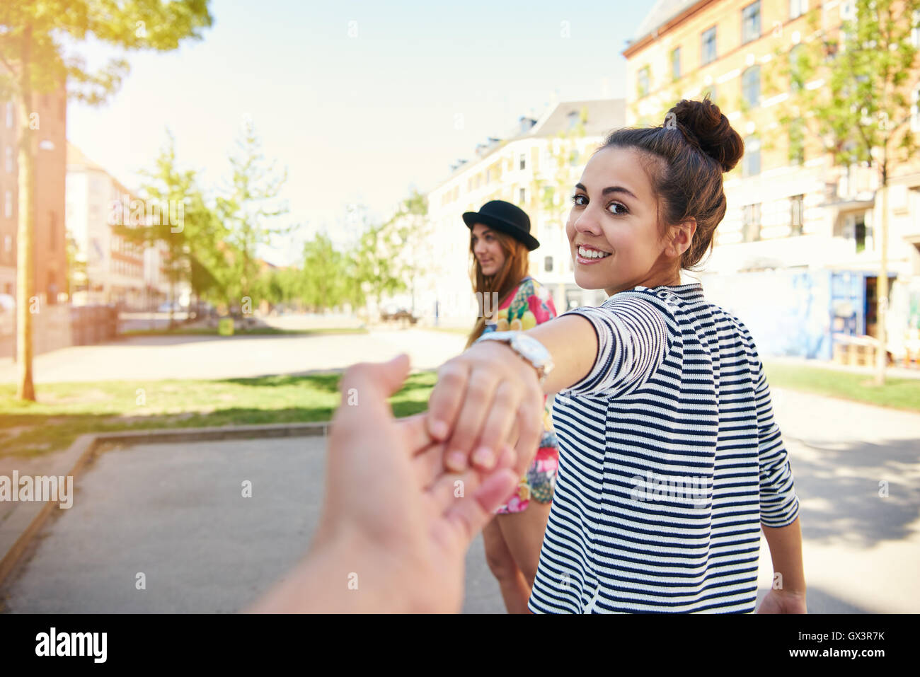 Pretty young woman pulling a man along by the hand turning to look back ...