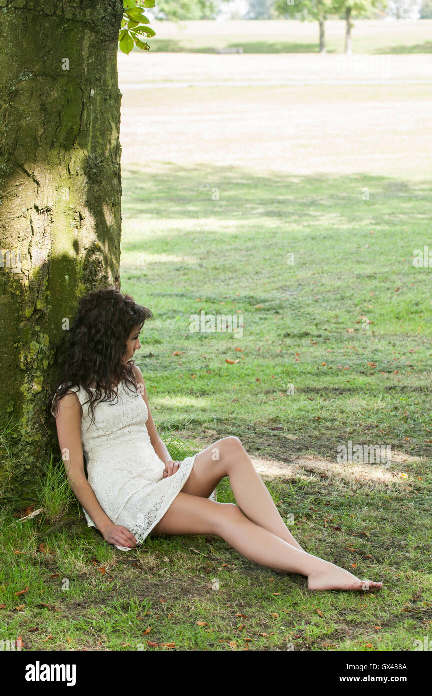 Sad young woman sitting against a tree outdoors Stock Photo - Alamy
