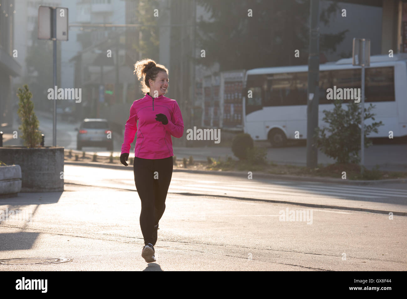 sporty woman running on sidewalk at early morning jogging with city ...
