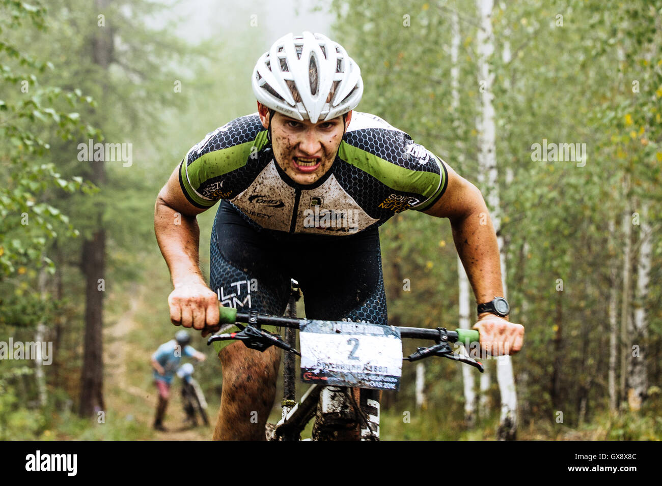 closeup of a male cyclist rides through forest, he has a dirty face ...
