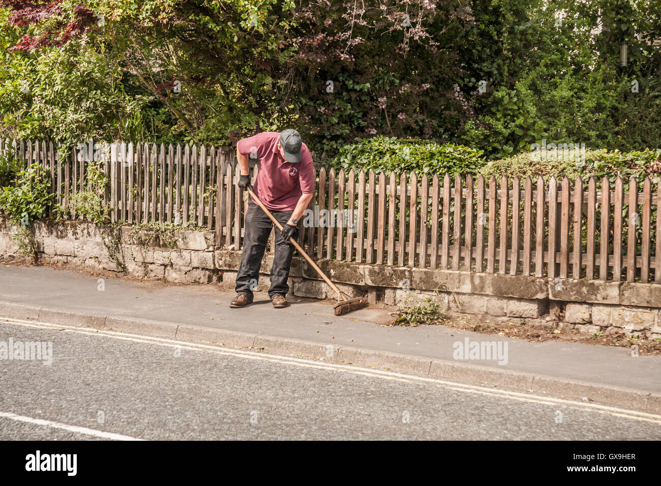 Middle aged man sweeping the pavement at Helmsley in North Yorkshire ...