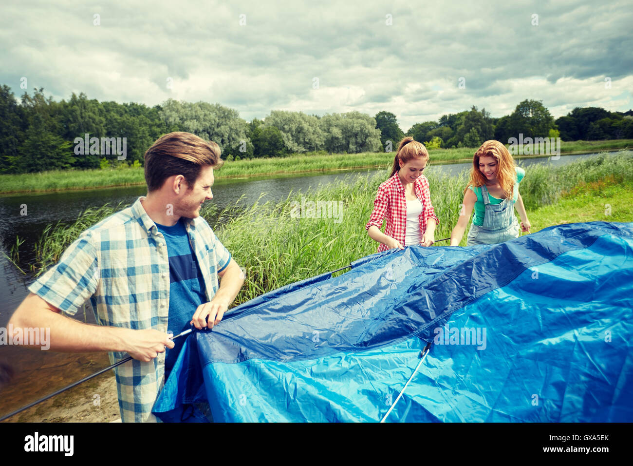 group of smiling friends setting up tent outdoors Stock Photo - Alamy