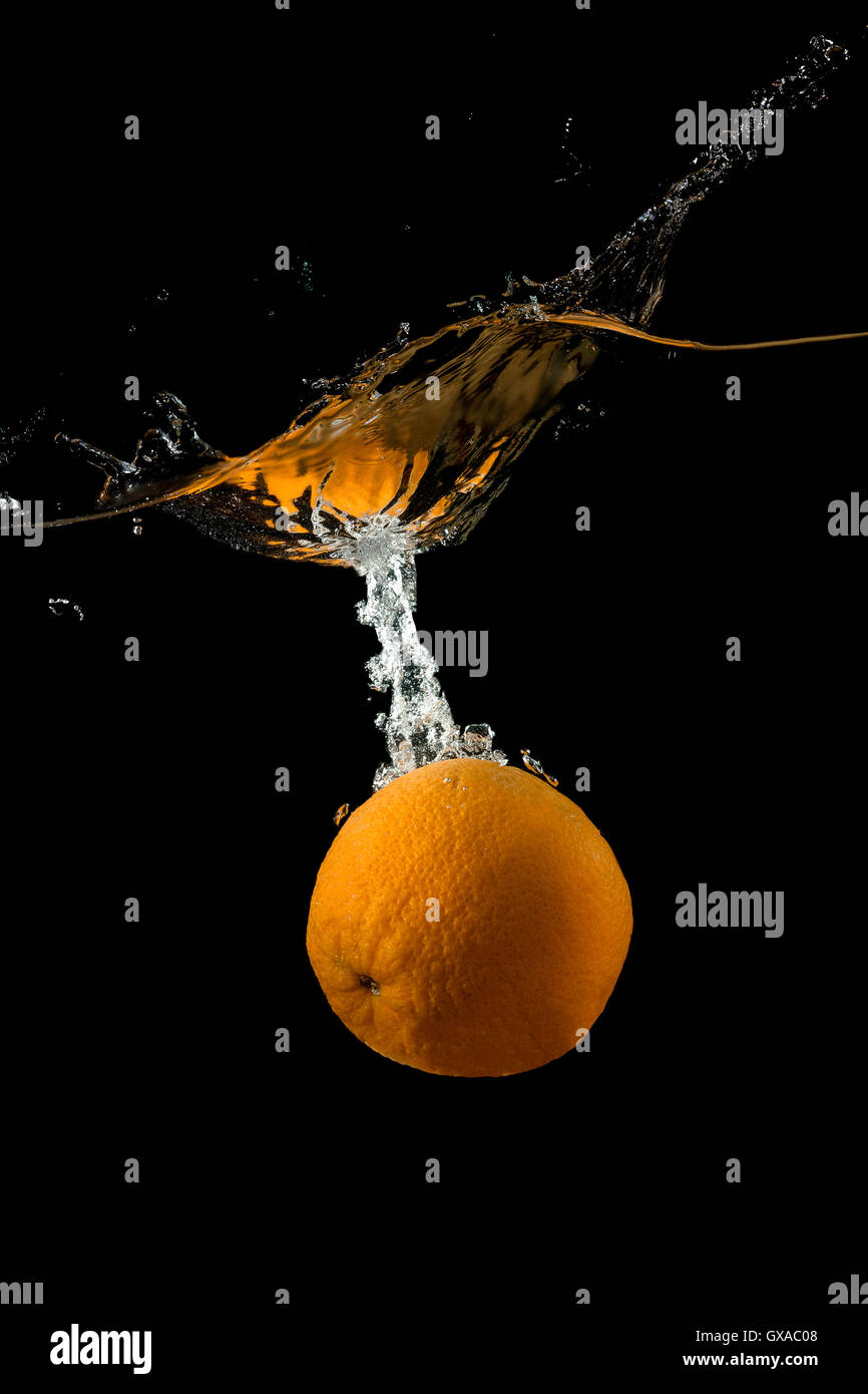 Orange falling into the water holding up a lot of splashes on a dark ...