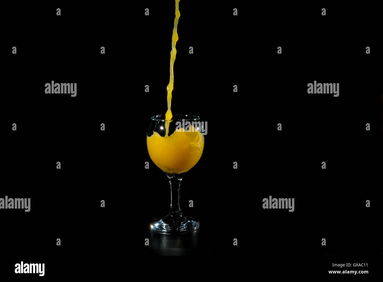 jet orange juice being poured into a glass beaker on a black background ...