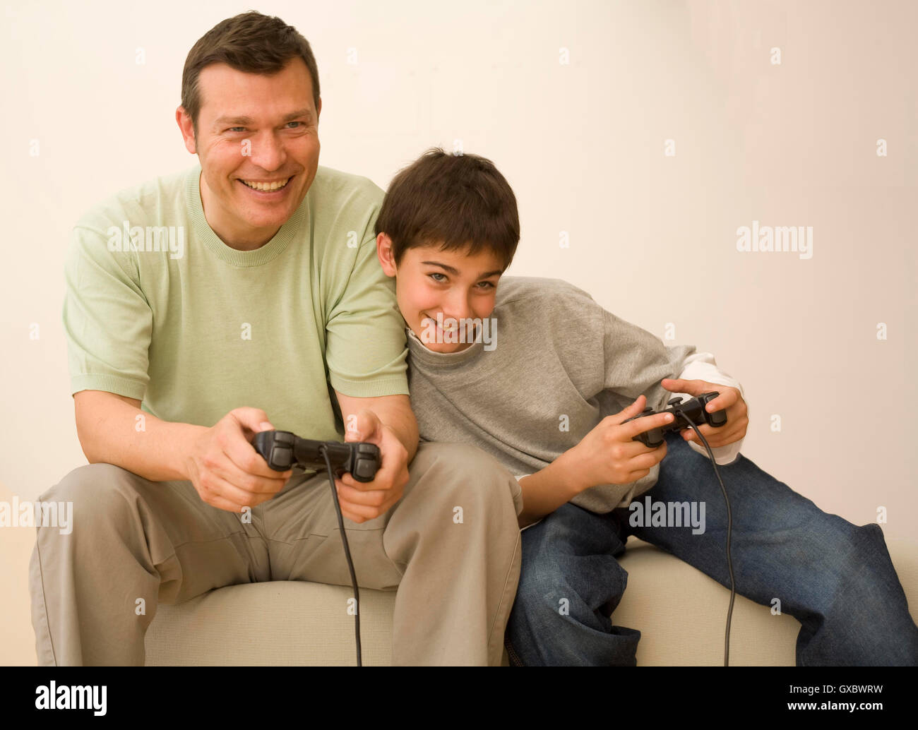 Boy and father playing with video game controllers on sofa Stock Photo ...
