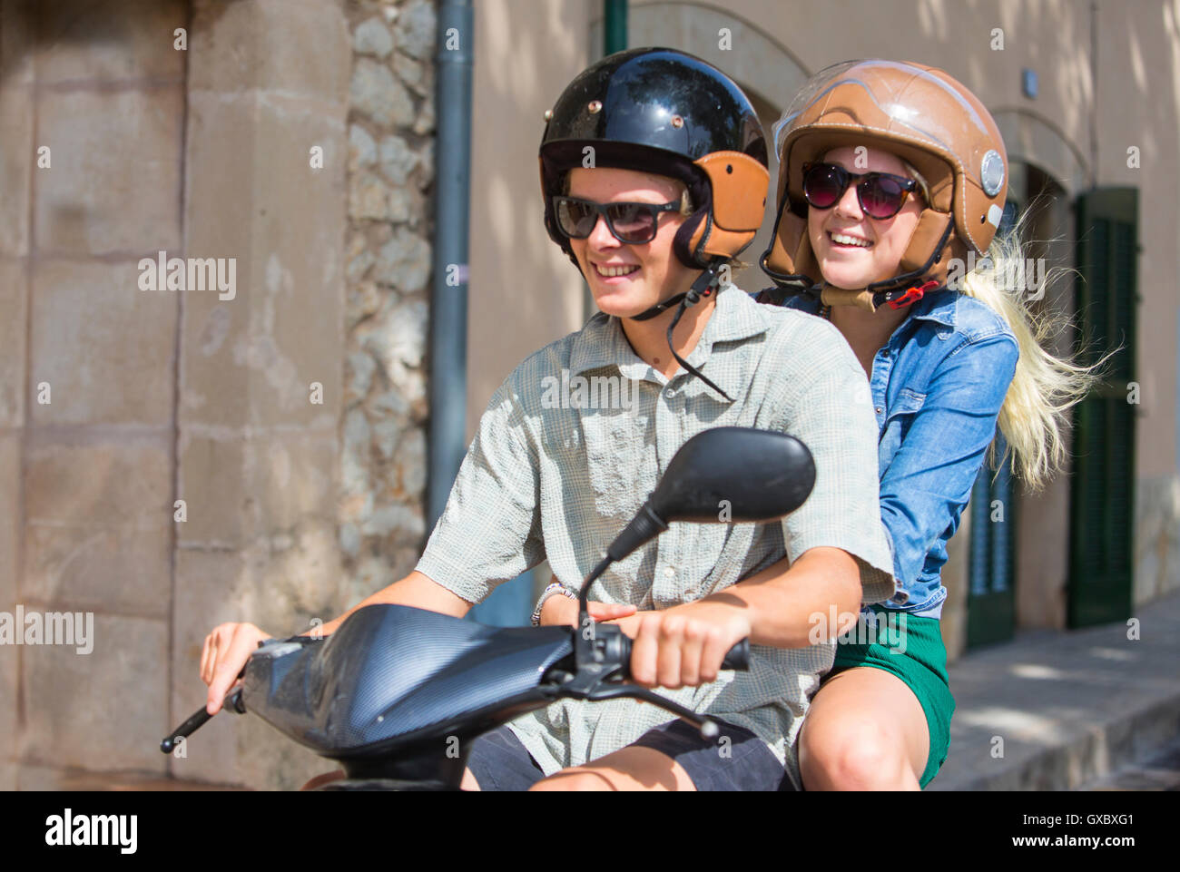 Young couple riding moped together through village, Majorca, Spain ...