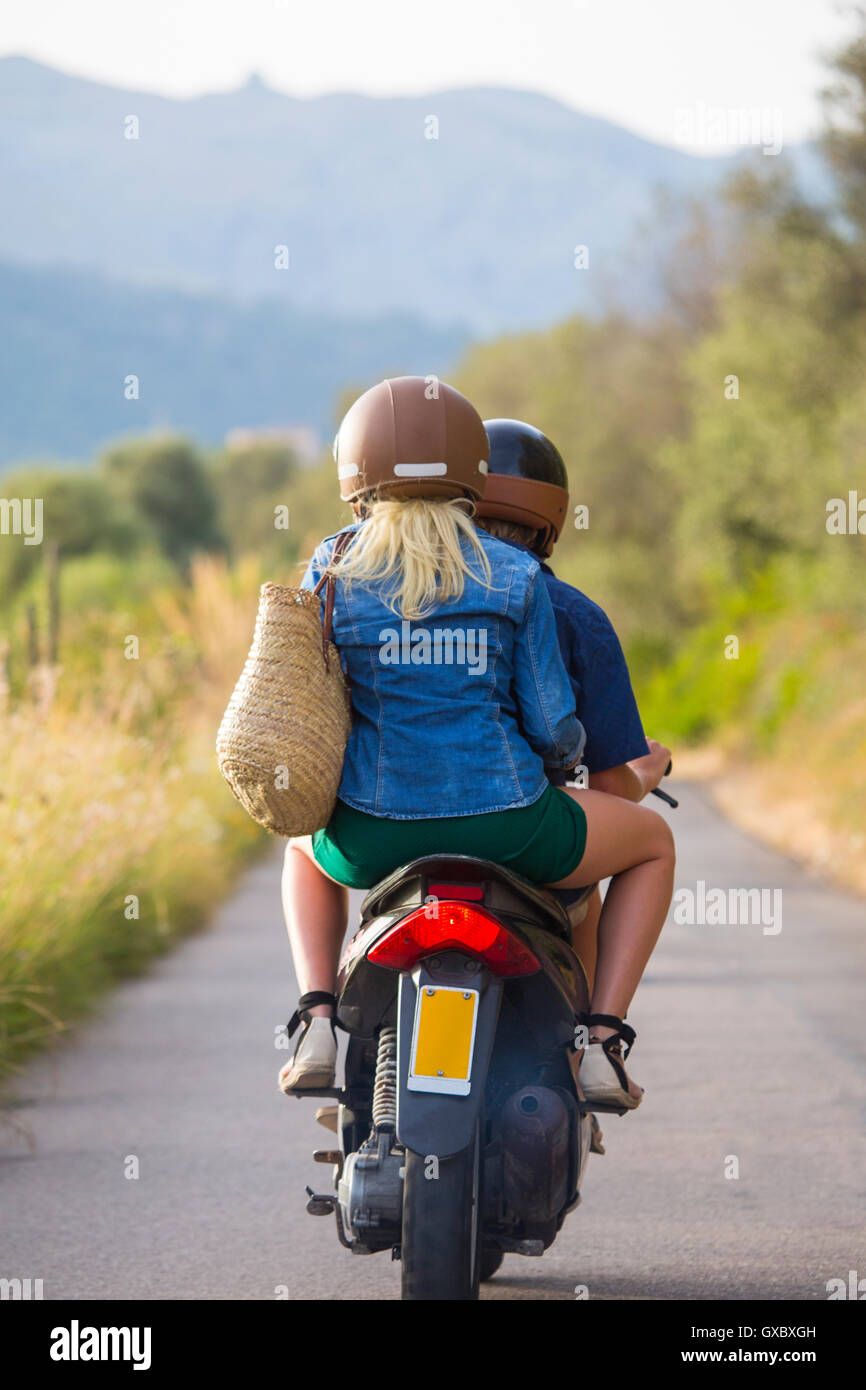 Rear view of young couple riding moped on rural road, Majorca, Spain ...