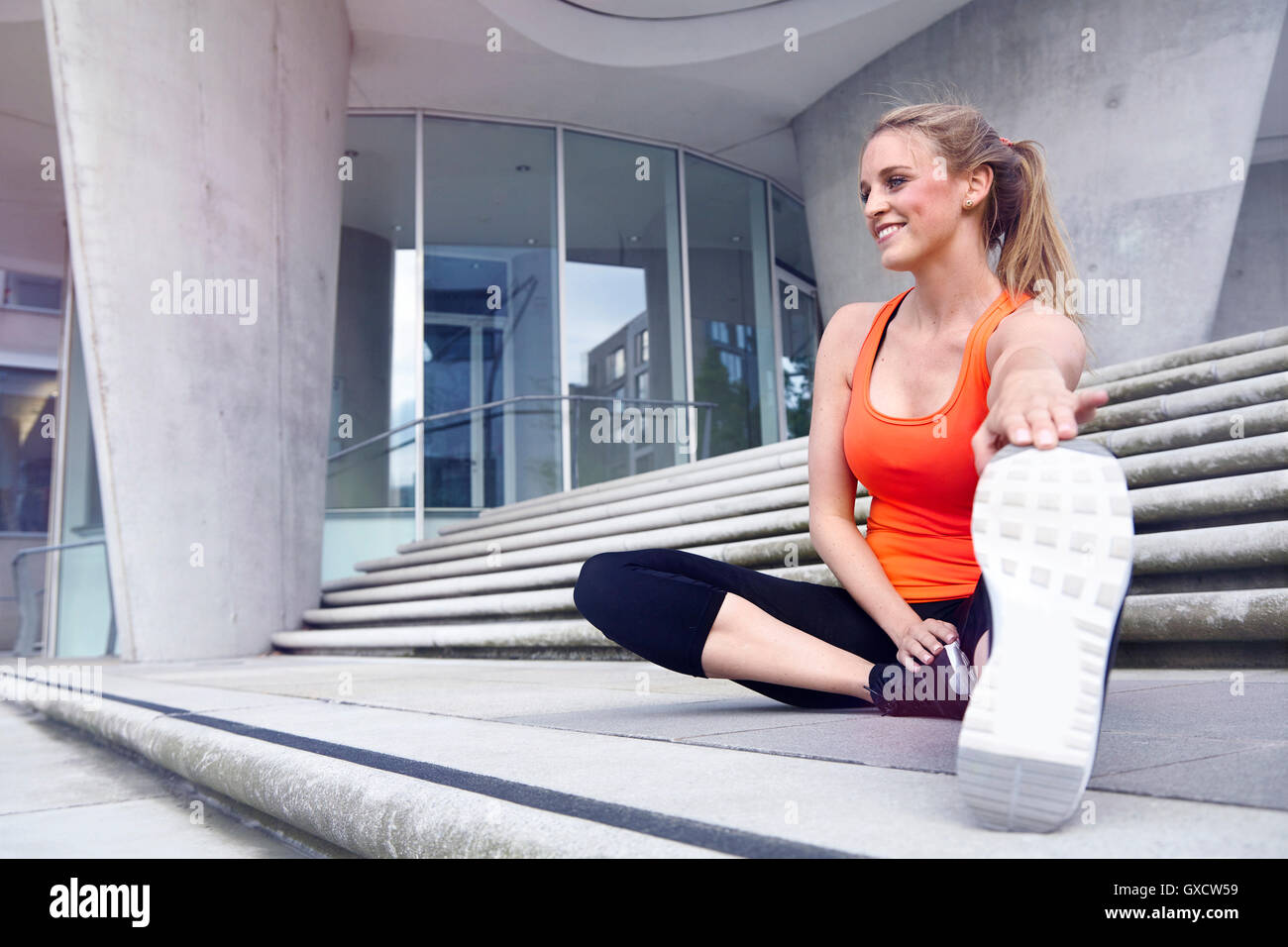 Woman sitting on steps stretching leg Stock Photo - Alamy