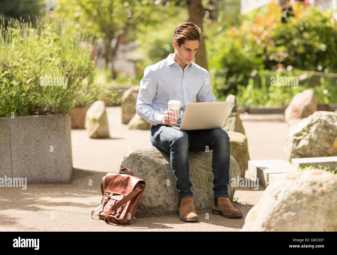 Young businessman reading laptop in city park Stock Photo - Alamy