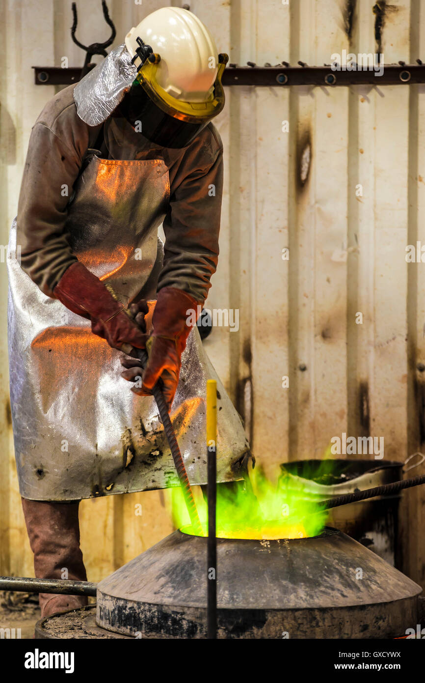 Male foundry worker working with green flamed furnace in bronze foundry ...