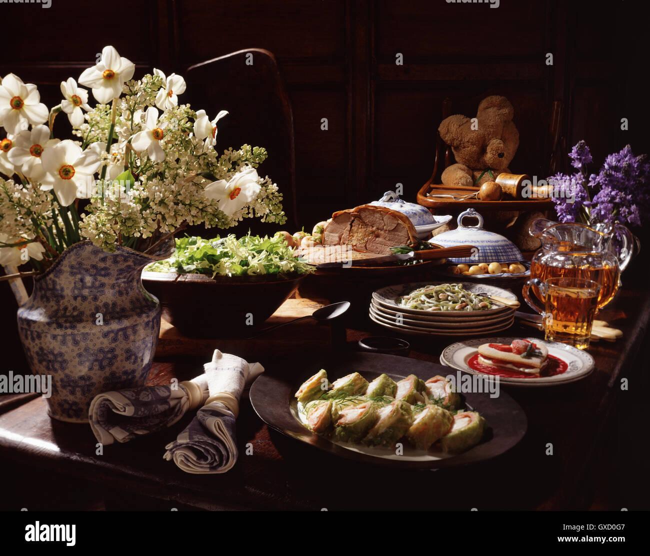 Traditional display of food; flowers in vase, roast lamb, potatoes ...