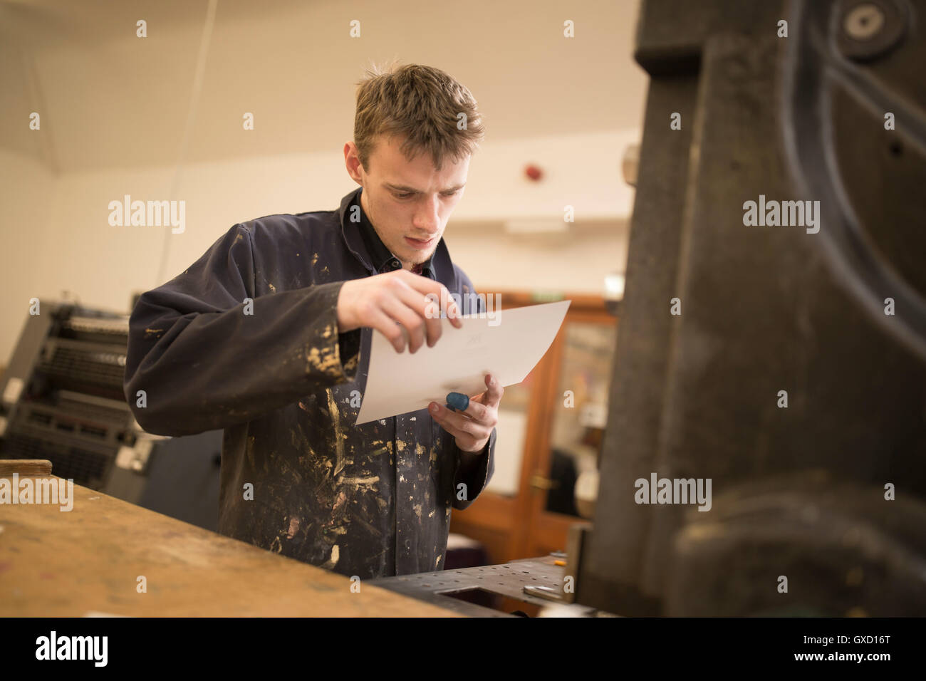 Young male printer inspecting paper for printing machinery in printing ...