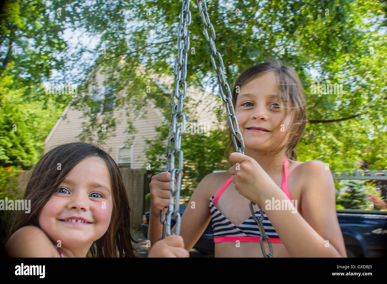 Portrait of two cute sisters playing on swing in garden Stock Photo - Alamy