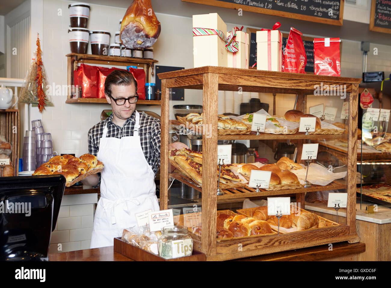 Male worker in bakery, putting fresh goods into display cabinet Stock ...