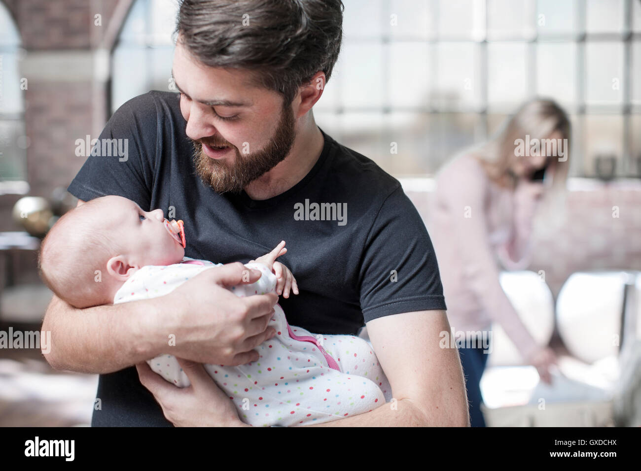 Father holding baby daughter, mother taking telephone call in ...