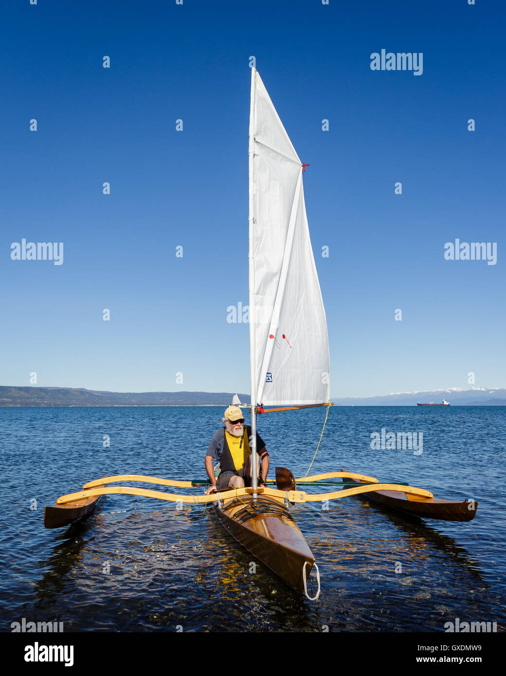 Man sails wooden outrigger sail boat on Homer spit on a beautiful day ...